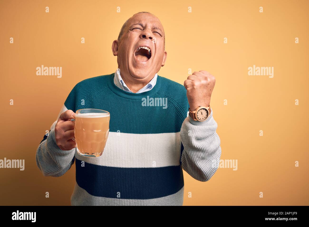 Senior handsome man drinking jar of beer standing over isolated yellow ...