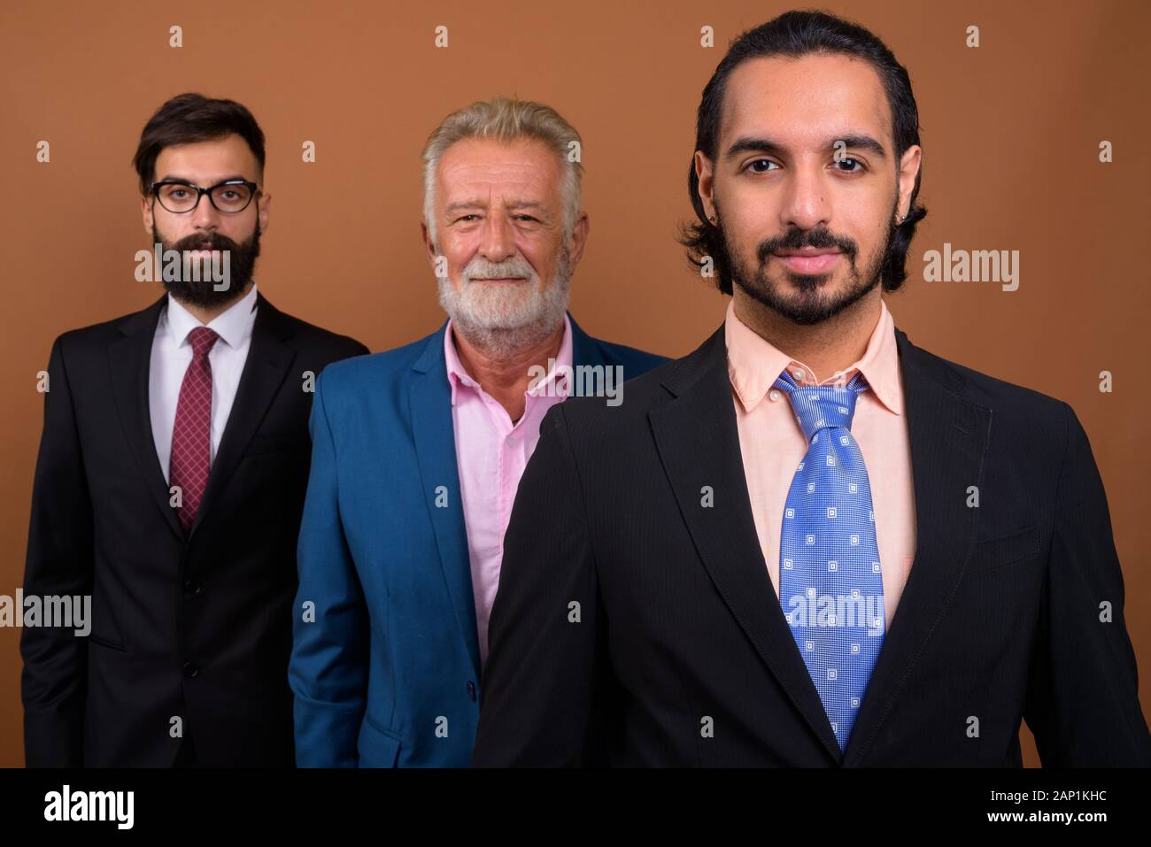 Three multi ethnic bearded businessmen together against brown ...