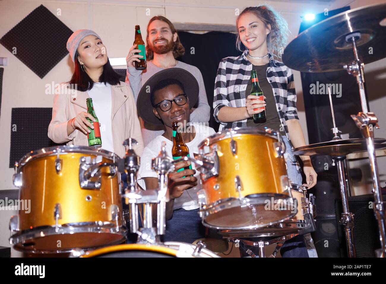 Portrait of multi-ethnic music band posing with beer bottles in studio ...