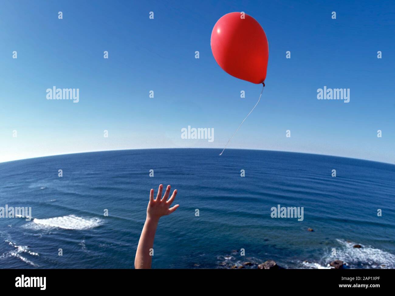 A boy releasing his red balloon over the Atlantic ocean, givingthe ...