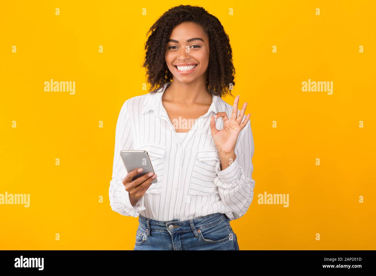 Portrait of smiling black woman using phone showing ok gesture Stock ...