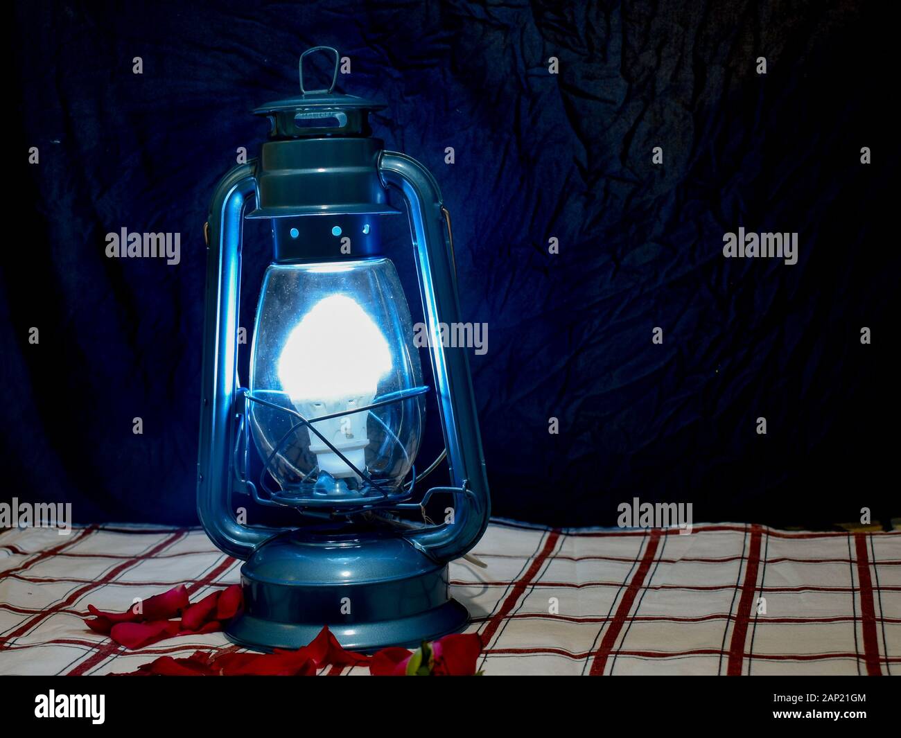a hurricane lamp on a patterned cloth with red rose petals spread at ...