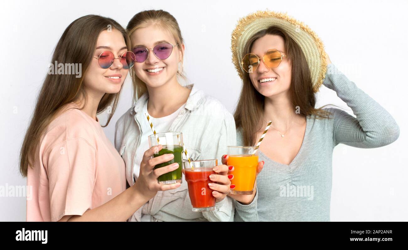Cheerful young girls in sunglasses drinking fresh healthy smoothie ...