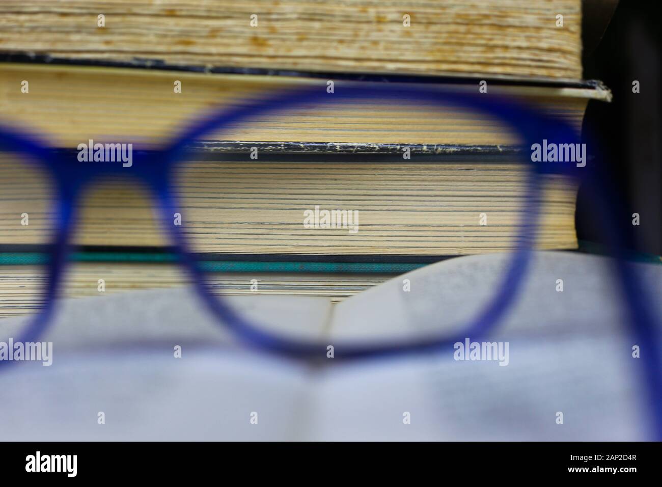 View through enlarging zoom lens of blue reading glasses on pile of ...