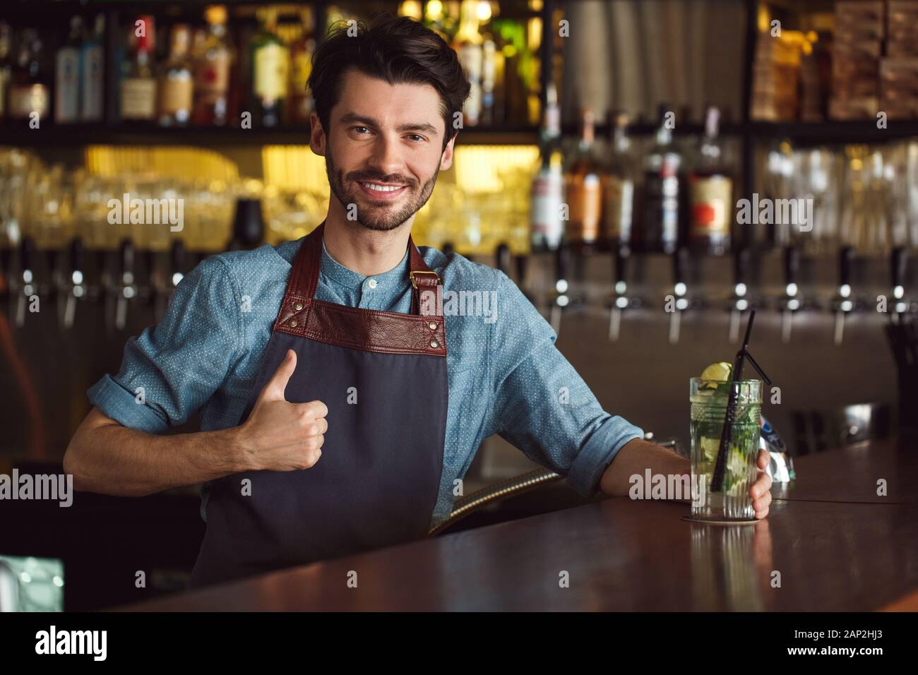 Professional Occupation. Bartender standing at counter serving mojito thumb up looking camera ...