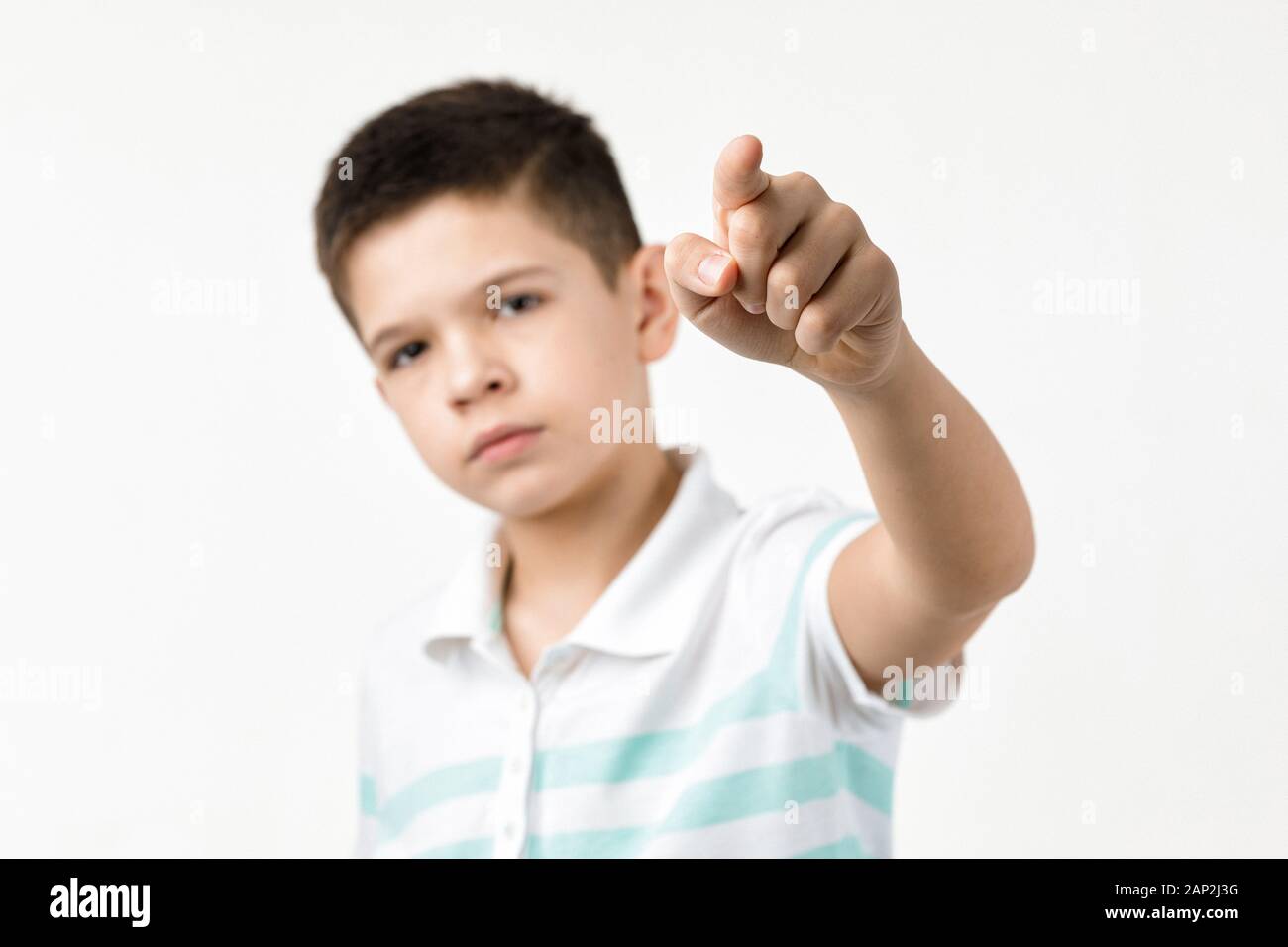 Cute little boy in striped t-shirt pointing camera on white background ...