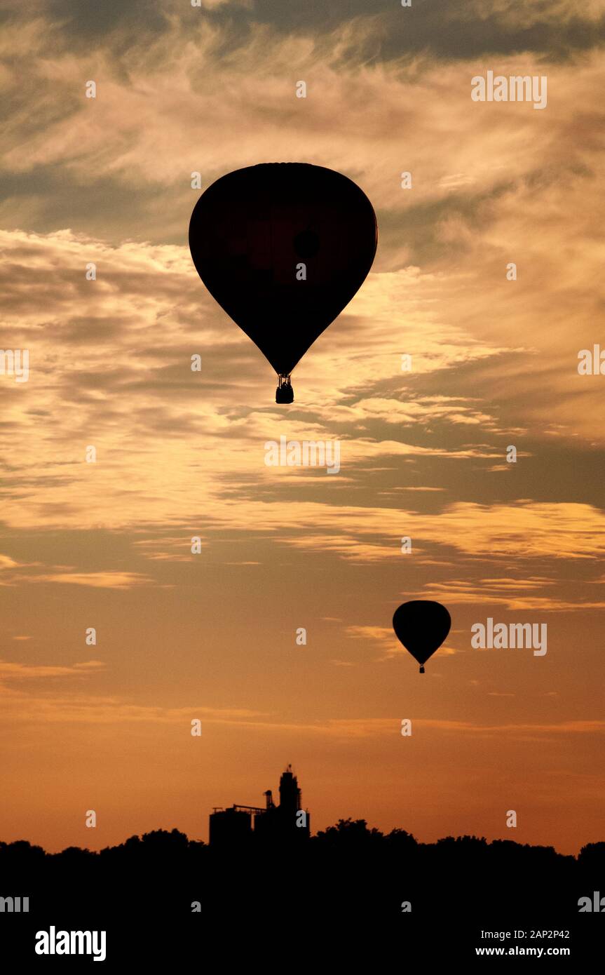 Two hot air balloons are silhouetted at sunset above an Iowa landscape ...