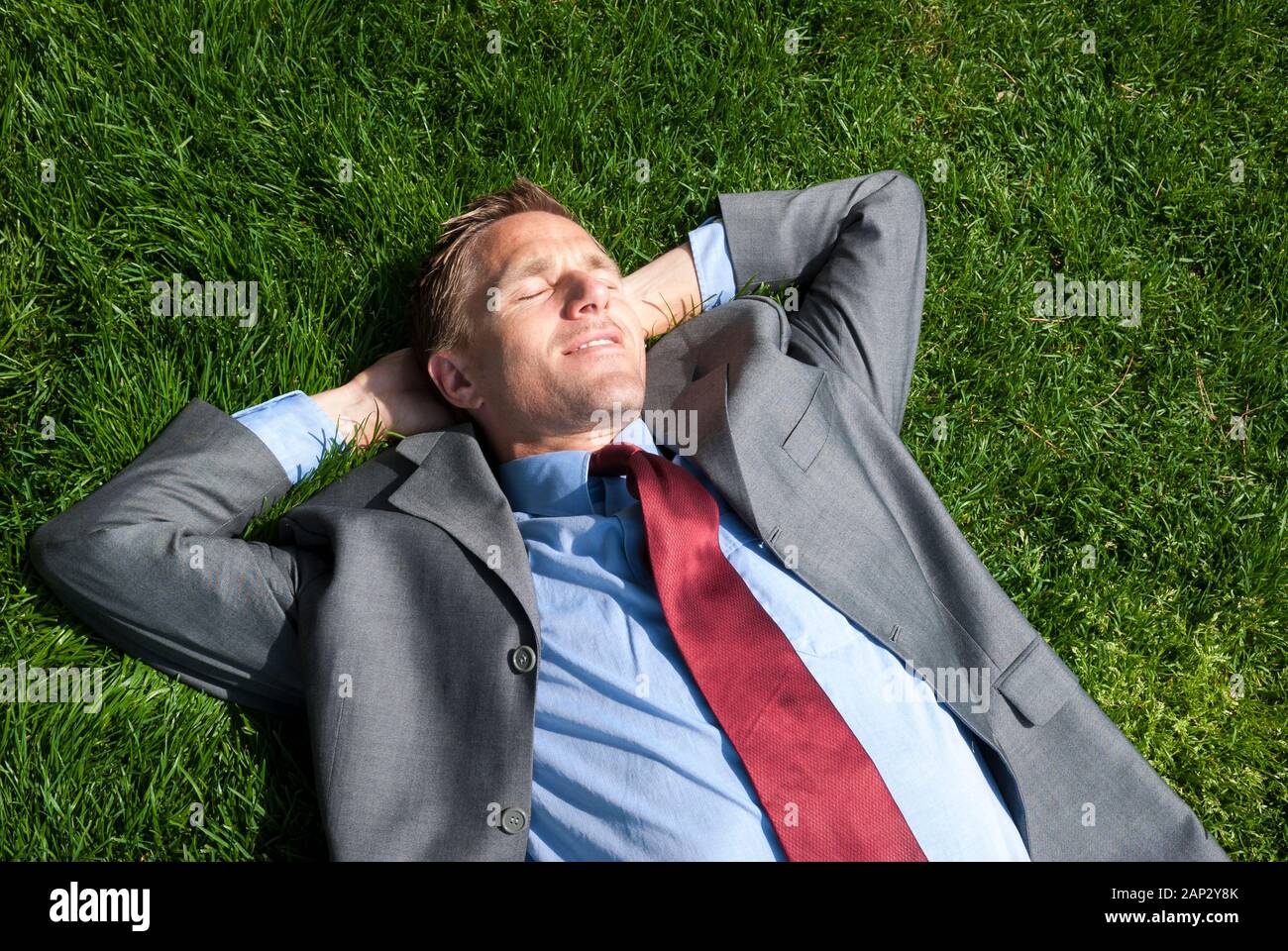 Tired businessman lying down outdoors taking a nap in bright green ...