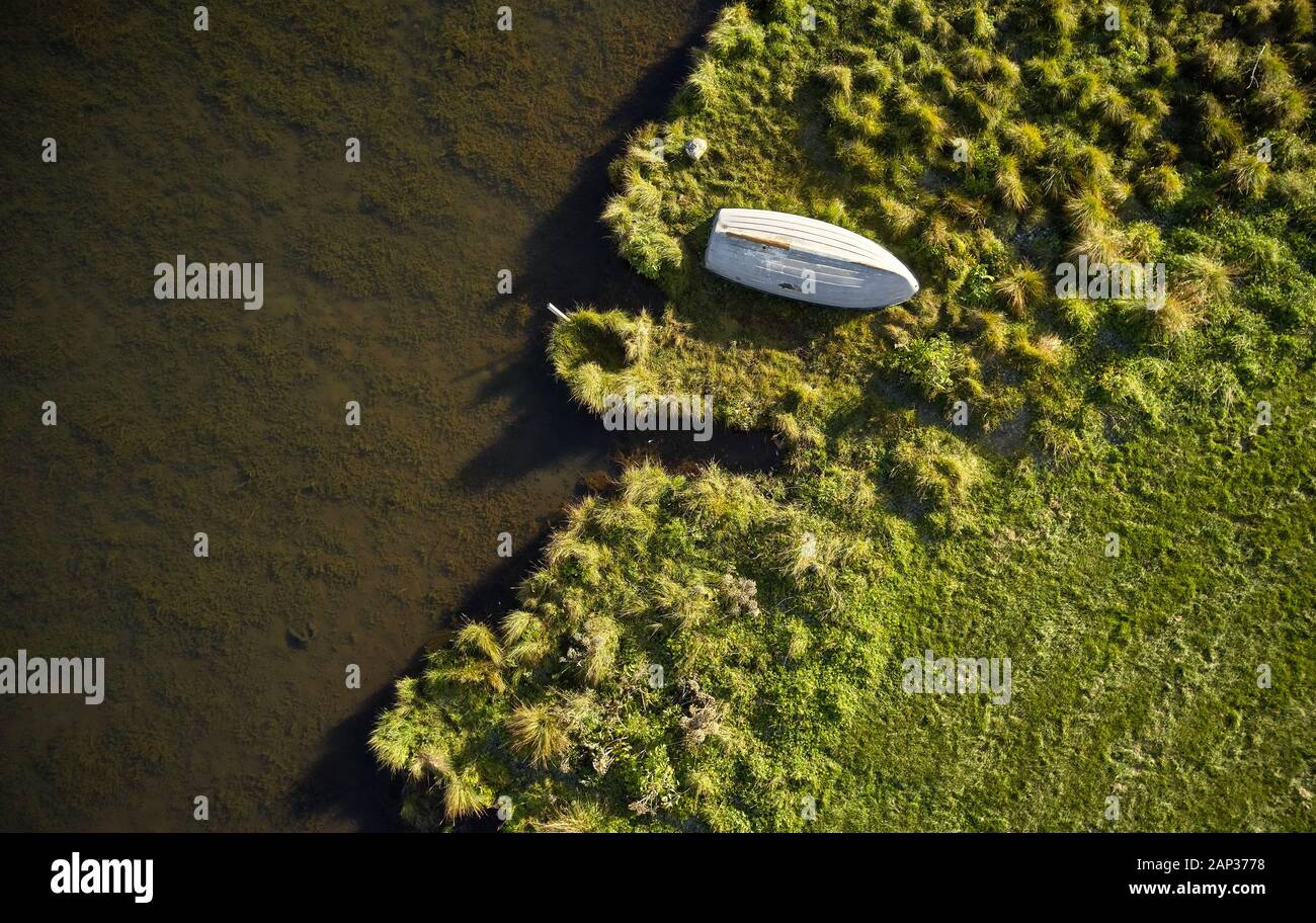 From above inverted wooden boat drying out on green grass on shore of ...