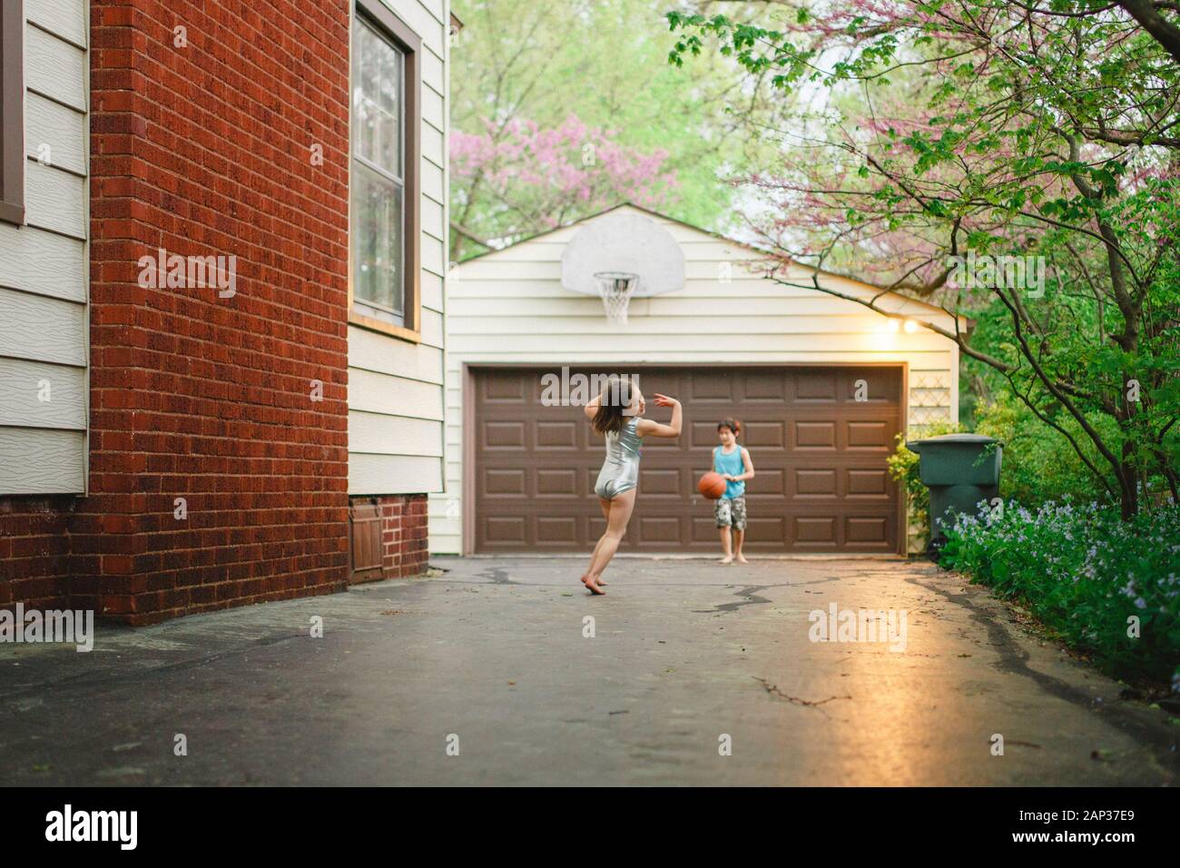 A little girl dances on a driveway while her brother plays basketball ...