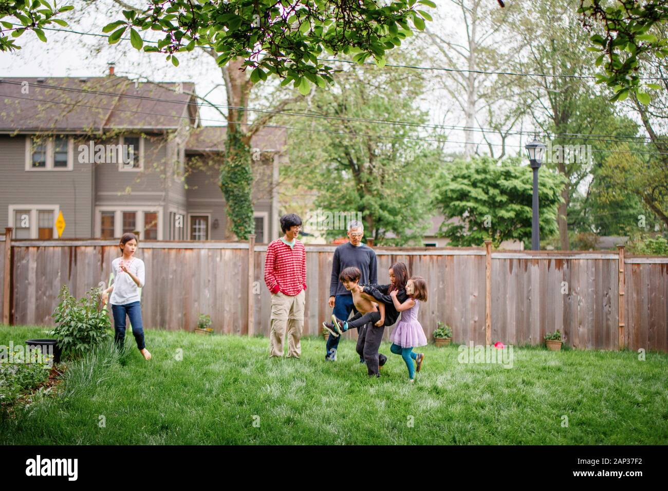 Two brothers play with their children in a suburban fenced-in backyard ...
