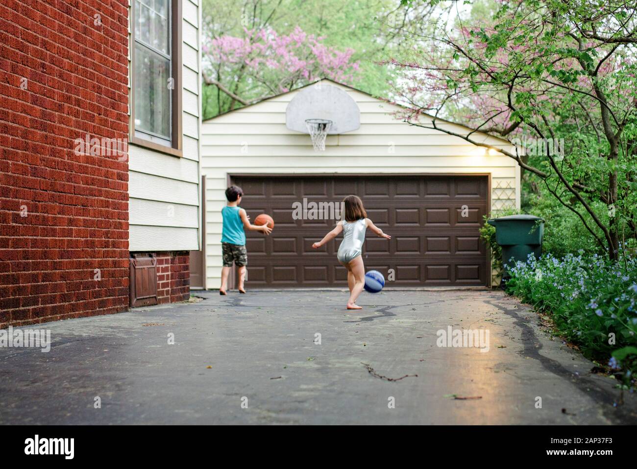 Two small children play basketball together in driveway at dusk Stock ...