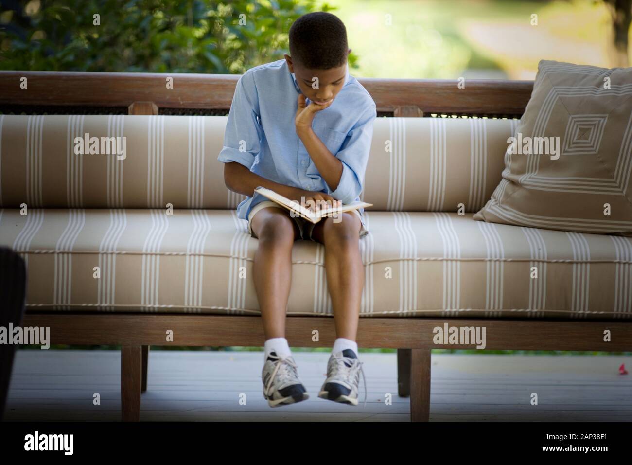 Boy sitting on a couch reading Stock Photo - Alamy