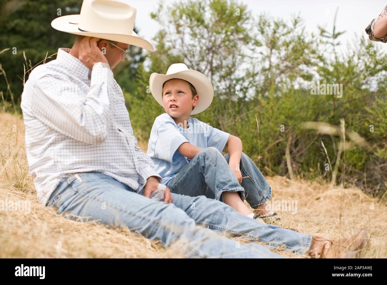 Father and son wearing cowboy hats sitting and talking in grassy field ...