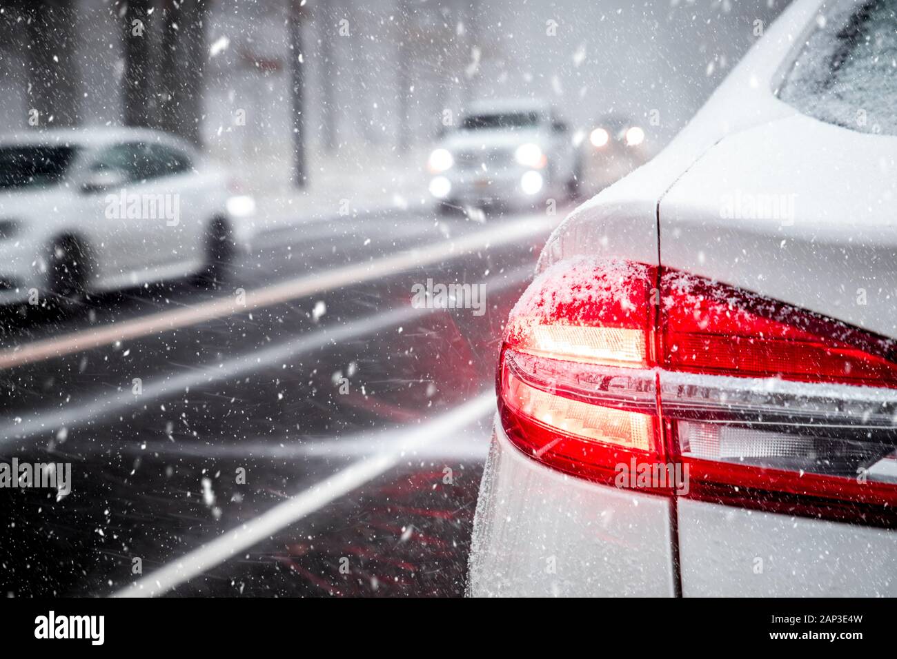 Rear red tail light on white car stopped on road during a snow storm ...