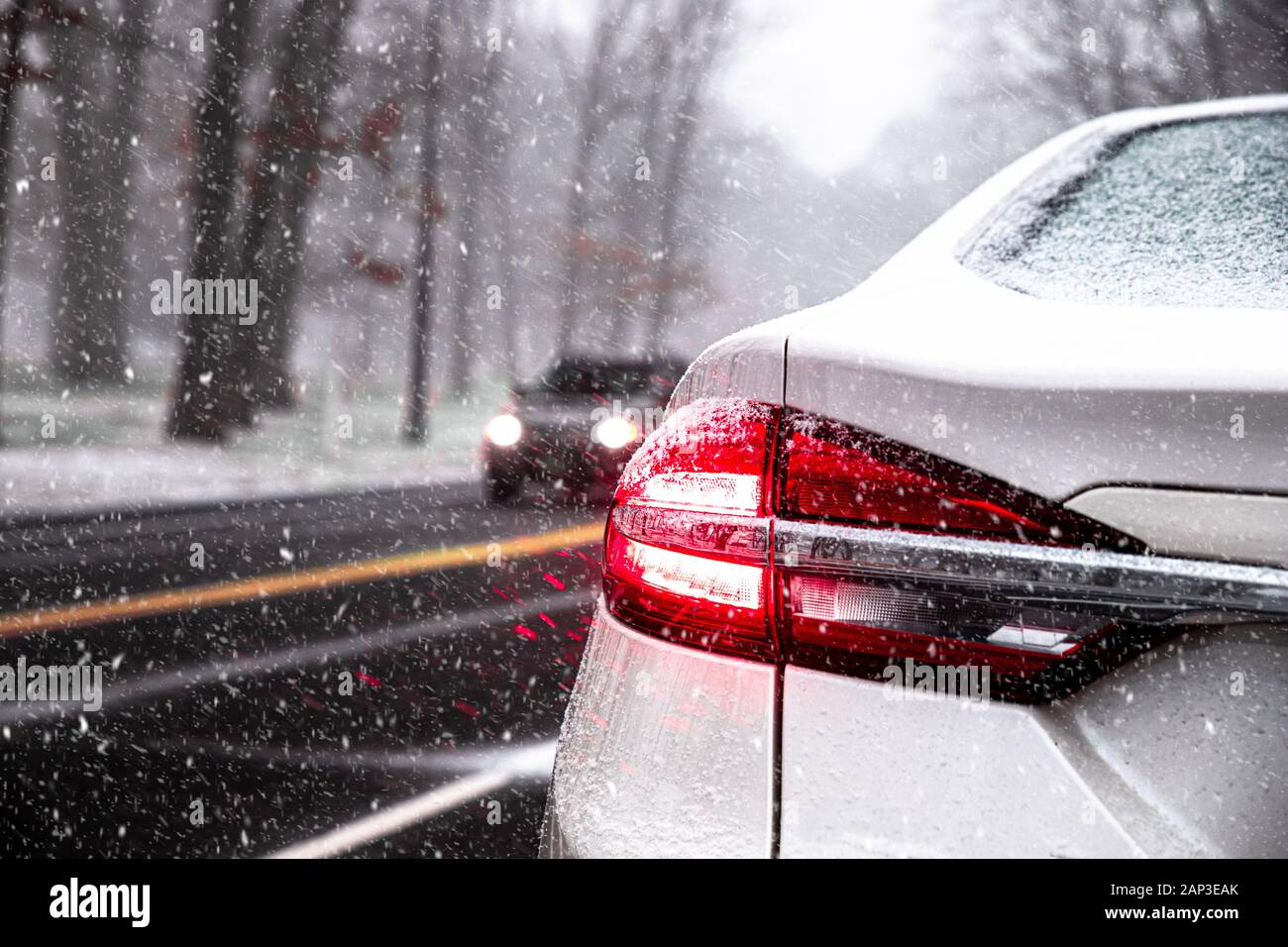 Rear red tail light on white car stopped on road during a snow storm ...