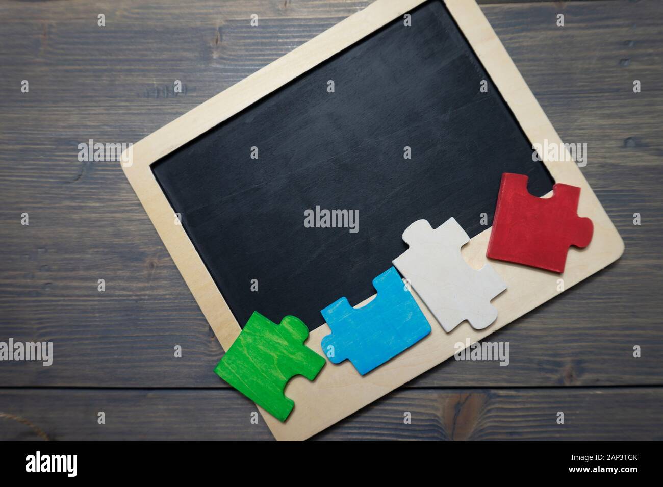 Colorful plywood puzzle pieces in green, blue, white and red on chalk ...