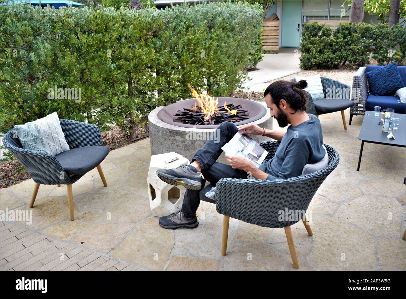 Caucasian young man with beard reading by fire pit in the cool morning ...