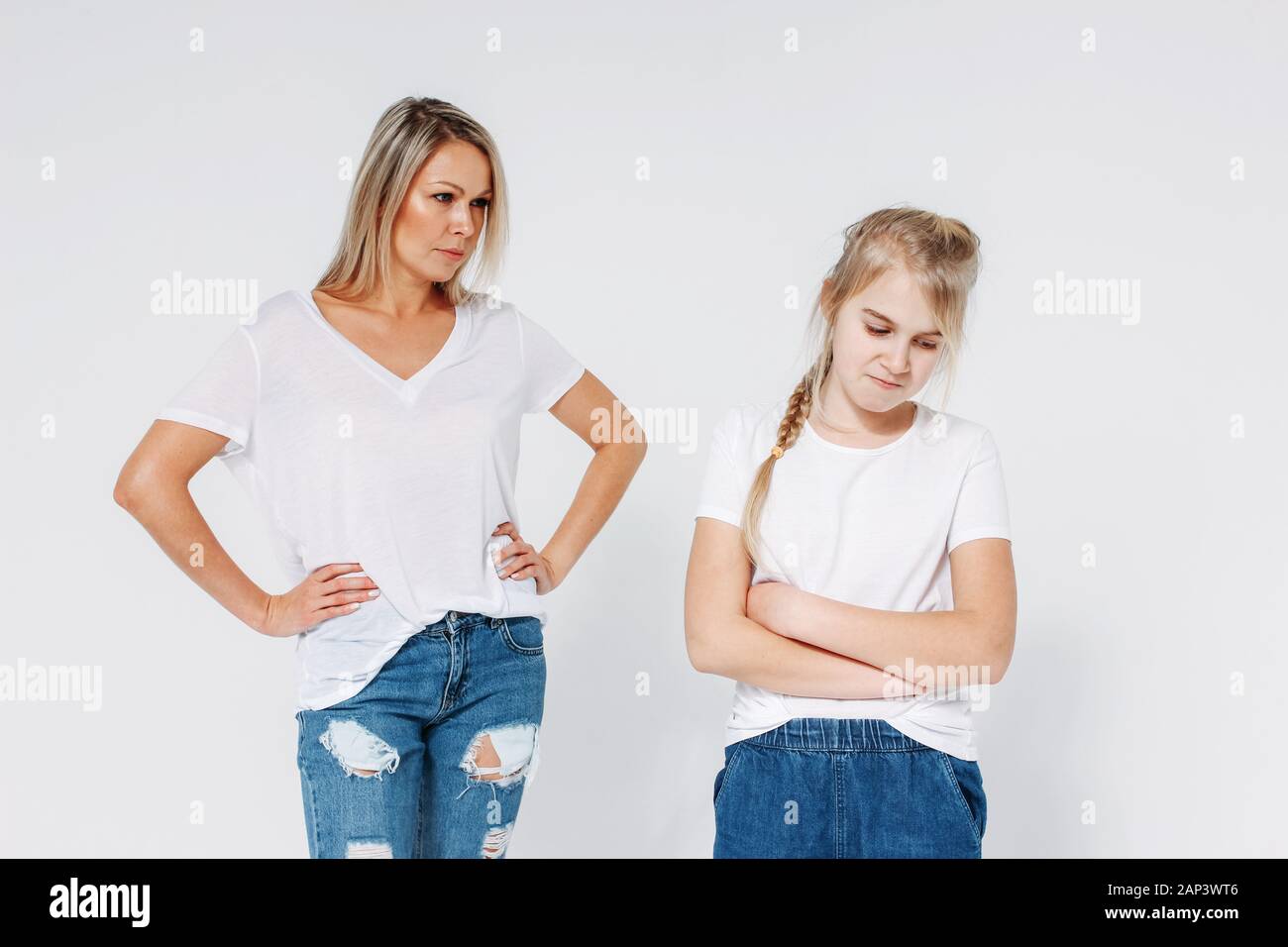 Blonde angry mom and sad daughter in white t-shirts and jeans isolated ...