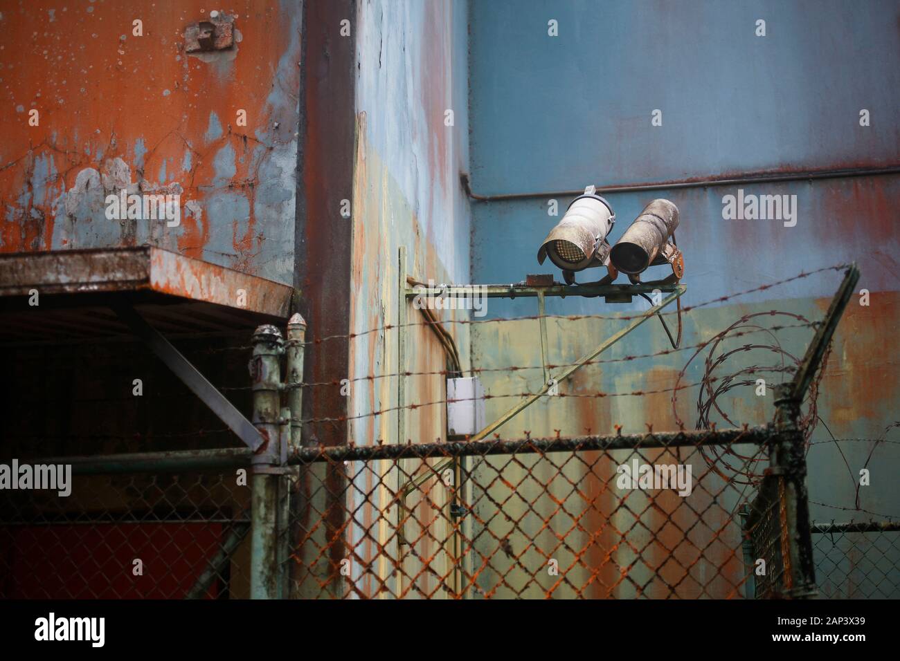 Surveillance cameras atop a chain link fence surrounding a rusty, aging ...