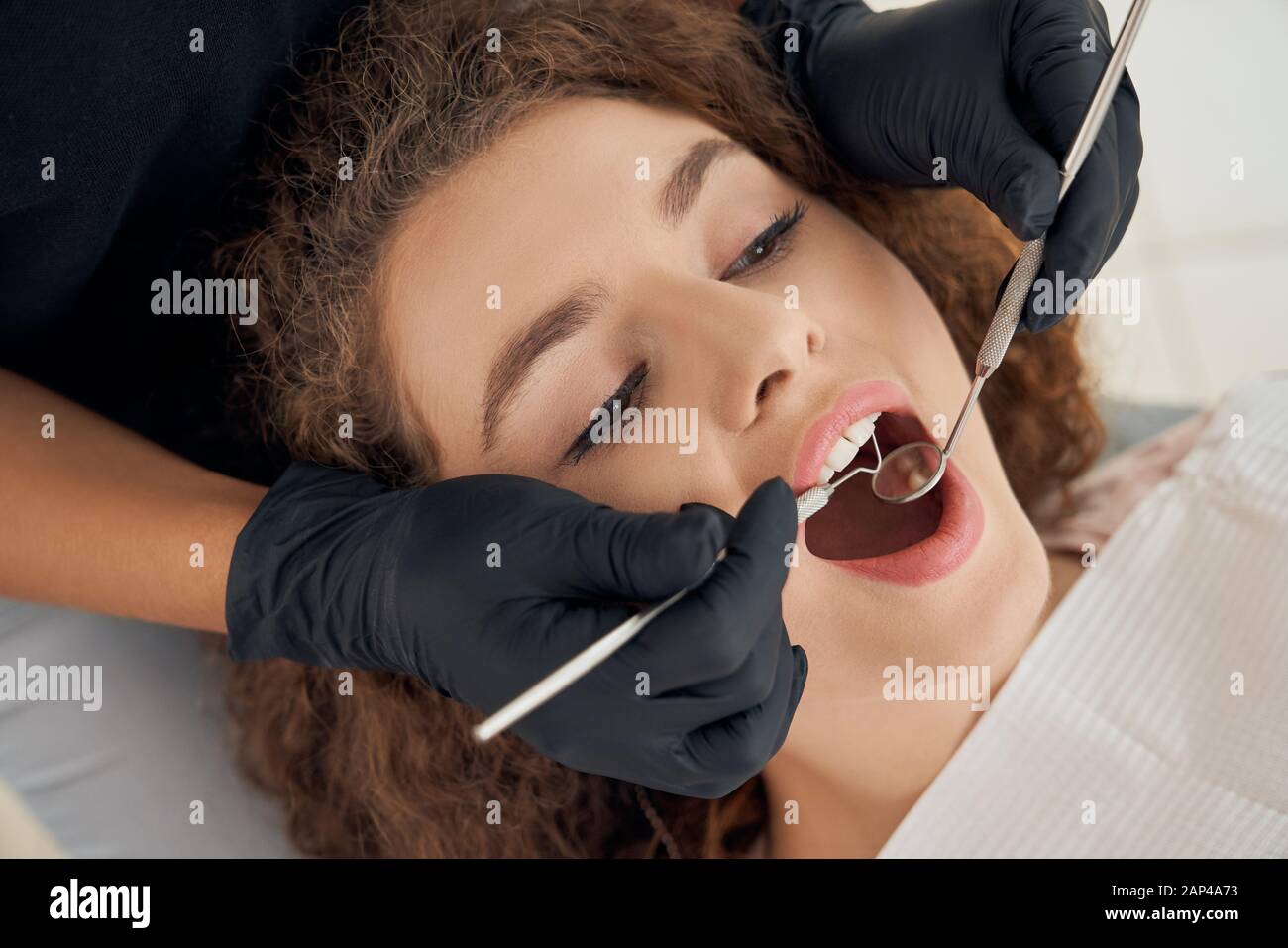 Competent dentist in black rubber gloves with dental mirror and probe ...