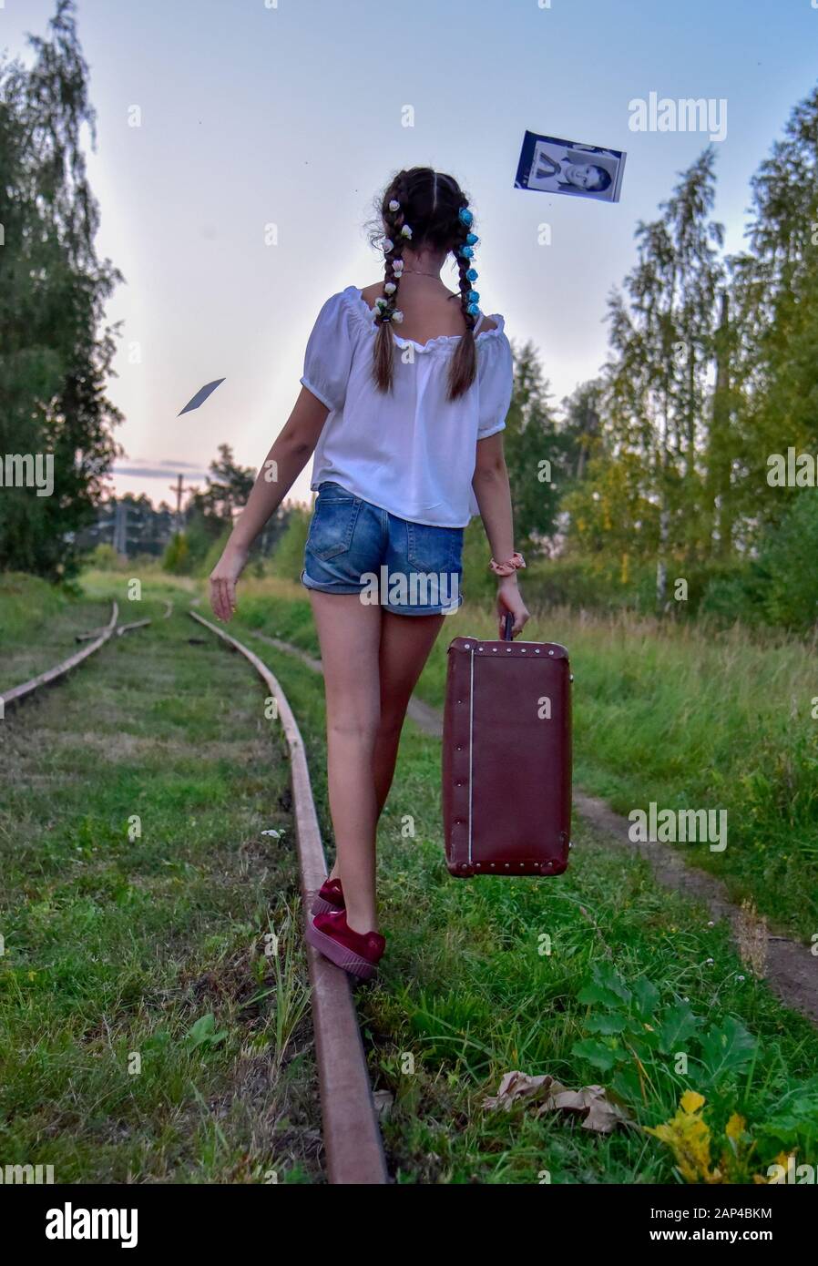 A teenage girl walks along the railway tracks with a heavy old suitcase ...