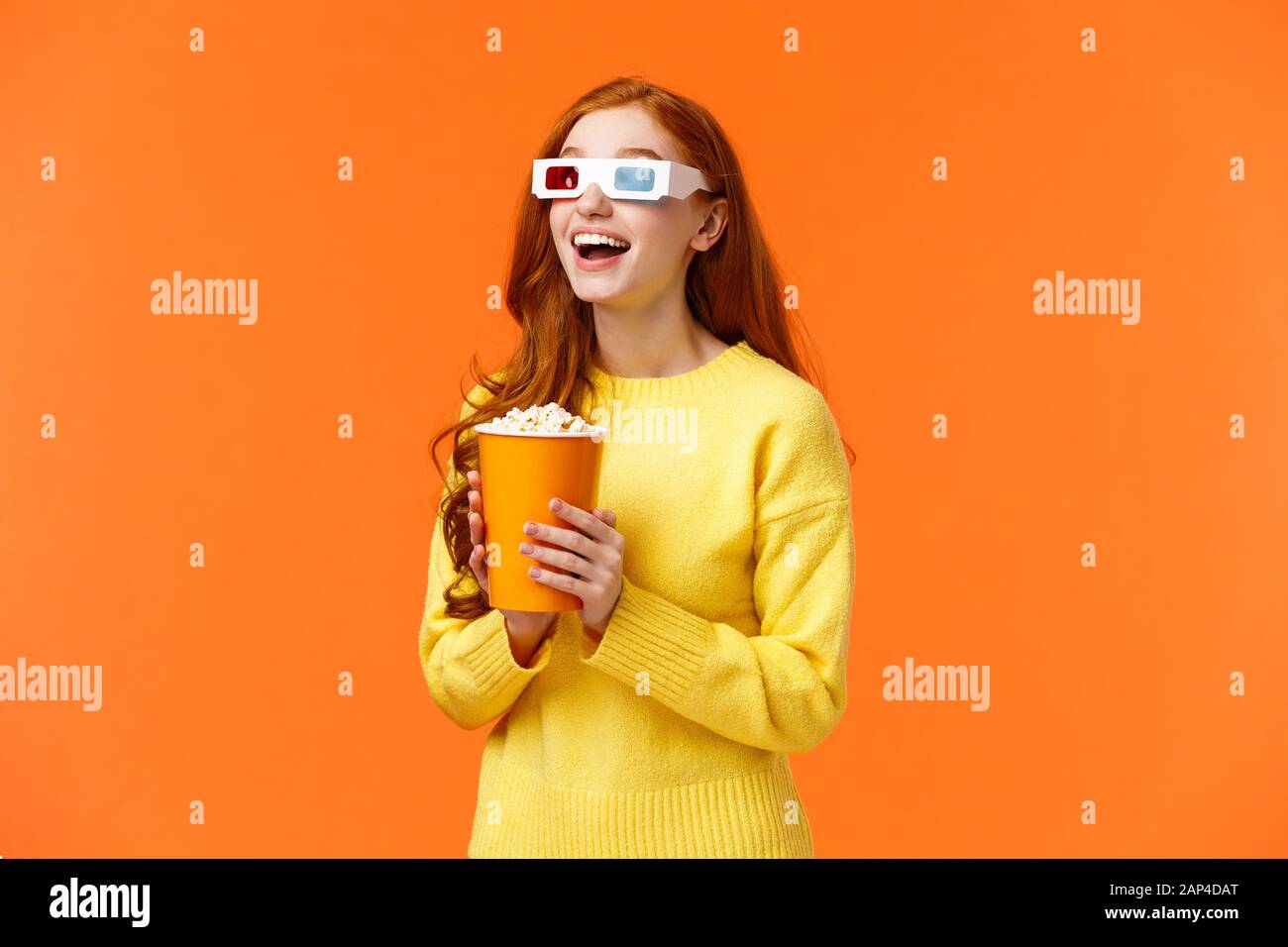 Girl eating popcorn, smiling amused as staring at large screen watching ...