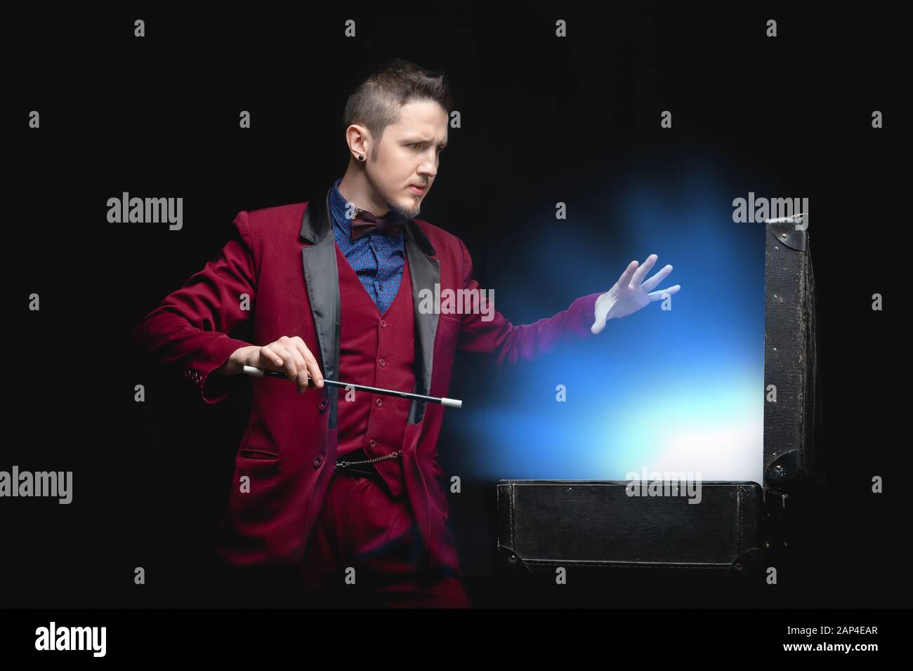 Magician man with magic wand shows disappearance in suitcase blue glow ...