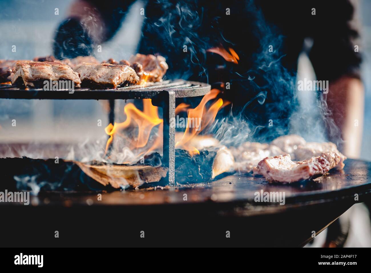 Cook grills steaks and pork ribs open fire. Turns meat over with tongs ...