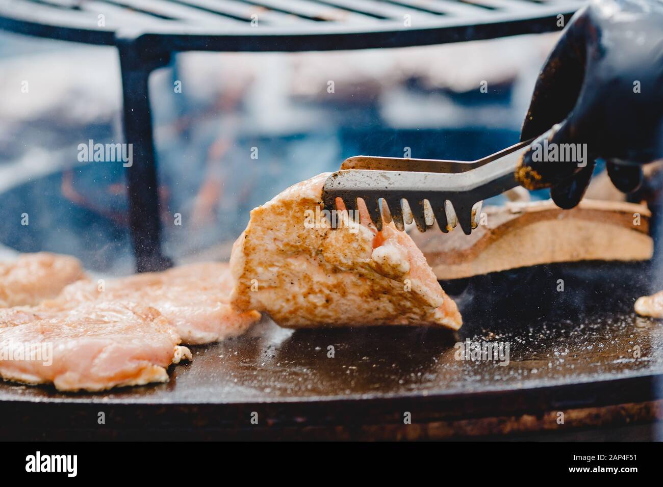 Cook grills steaks and pork ribs open fire. Turns meat over with tongs ...