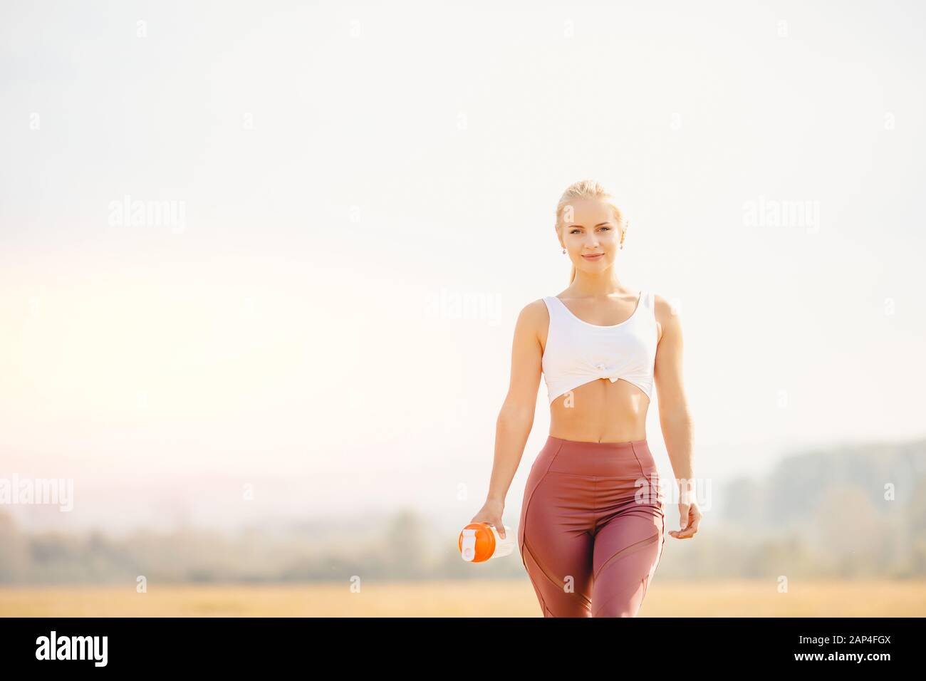 Beautiful athletic girl runner holds water bottle and looks into frame ...