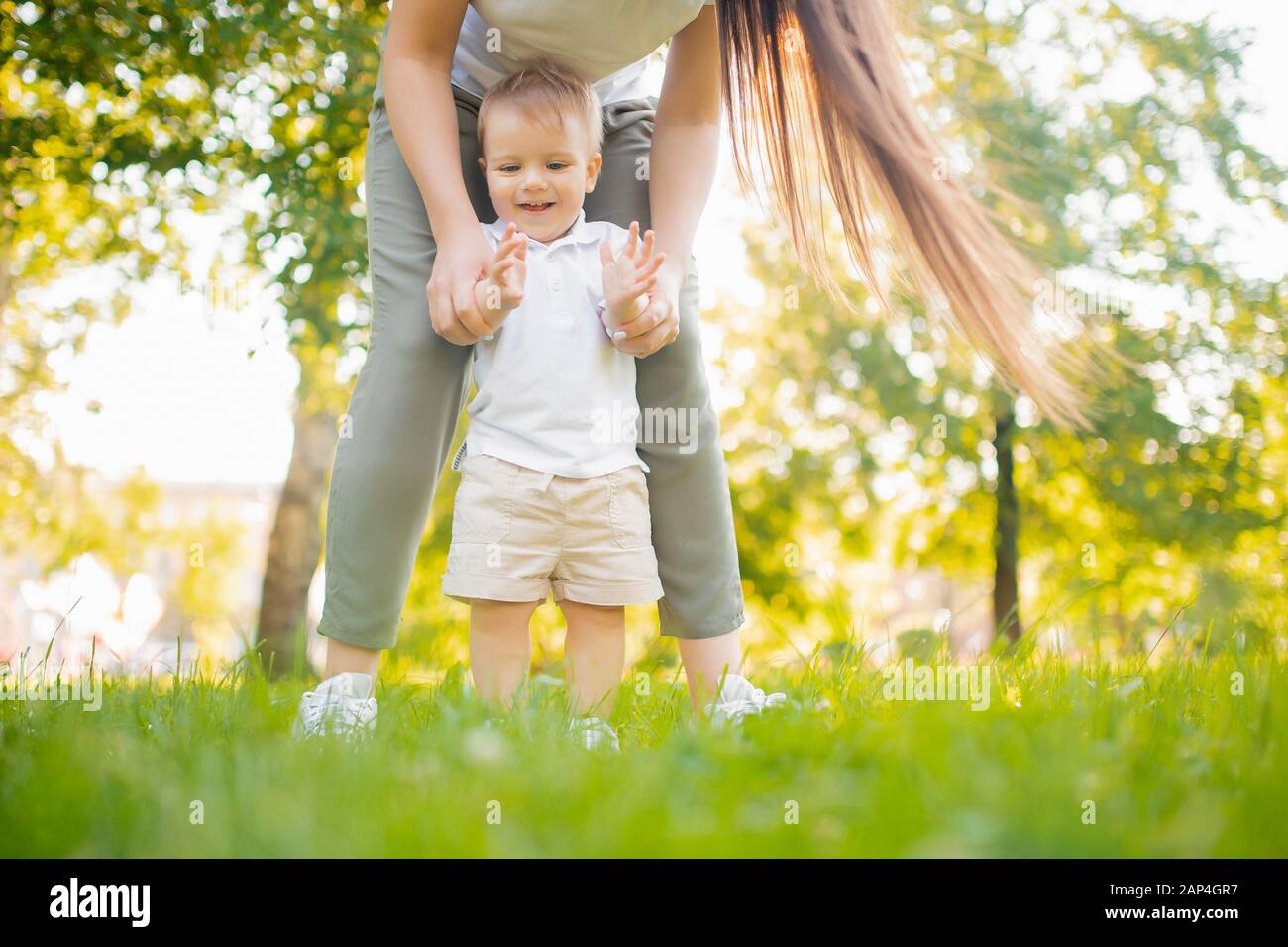 Happy smiling child boy makes first step in park, mom helps Stock Photo ...