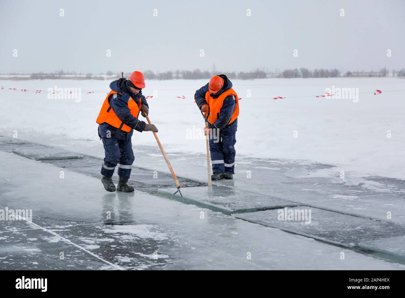 Workers rafting ice blocks along a channel cut out by a frozen lake ...