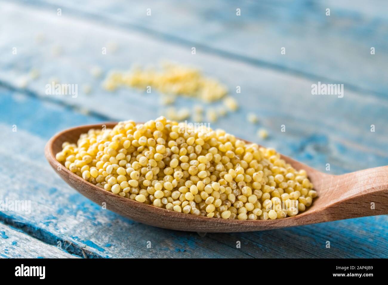 Dry yellow millet in a spoon against a background of old blue boards ...