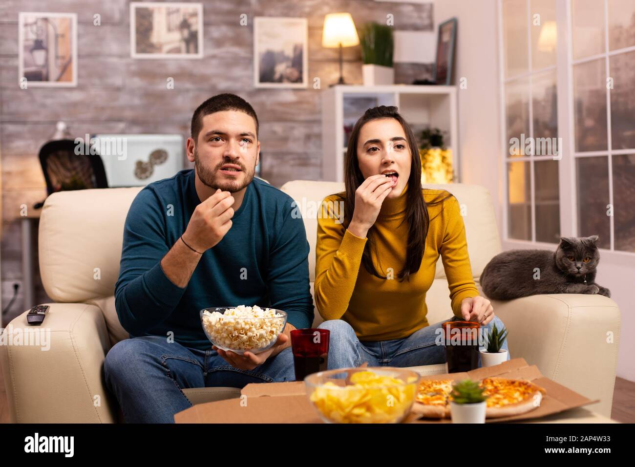 Beautiful young couple watching TV and eating fast food takeaway in the ...