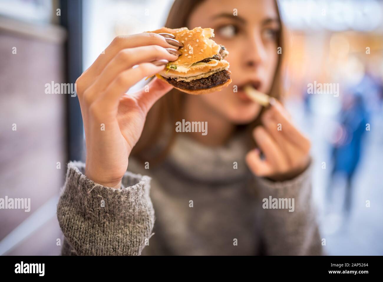 Beautiful young cute girl in jumper enjoys fast food hamburger while ...
