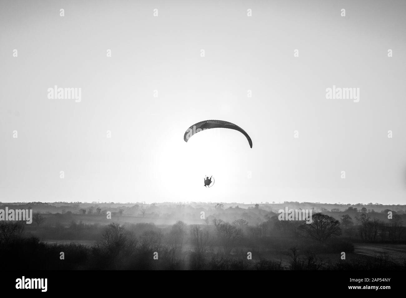Para-glider / paraglider flying in the sunset over fields and trees B&W ...