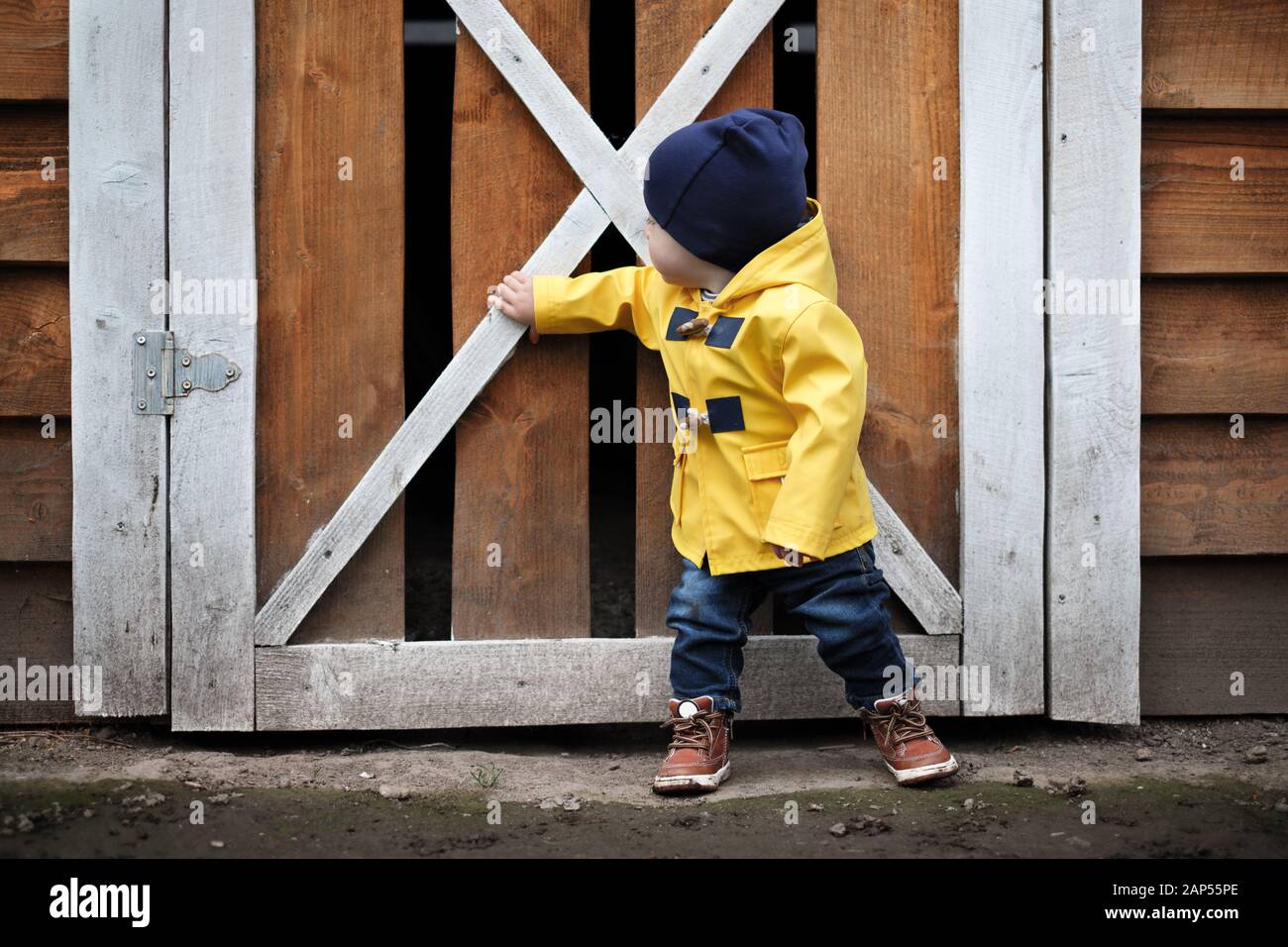 Small kid in yellow jacket near wooden barn Stock Photo - Alamy