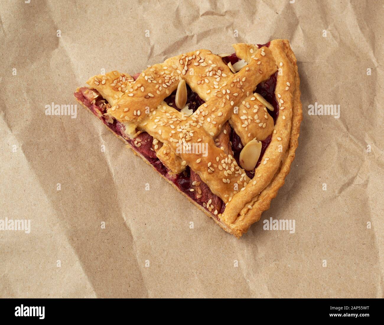 triangular slice of baked cherry pie on brown paper, top view, blue ...