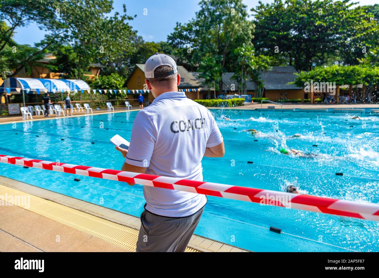 Back View Of A Male Coach In White Coach Shirt Watching His Swimmers