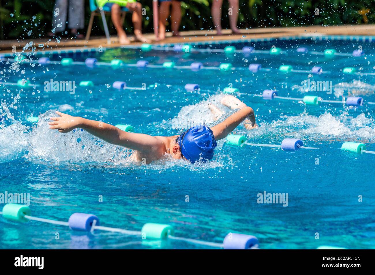 Young boy swimmer doing butterfly stroke at a pool on a bright sunny ...
