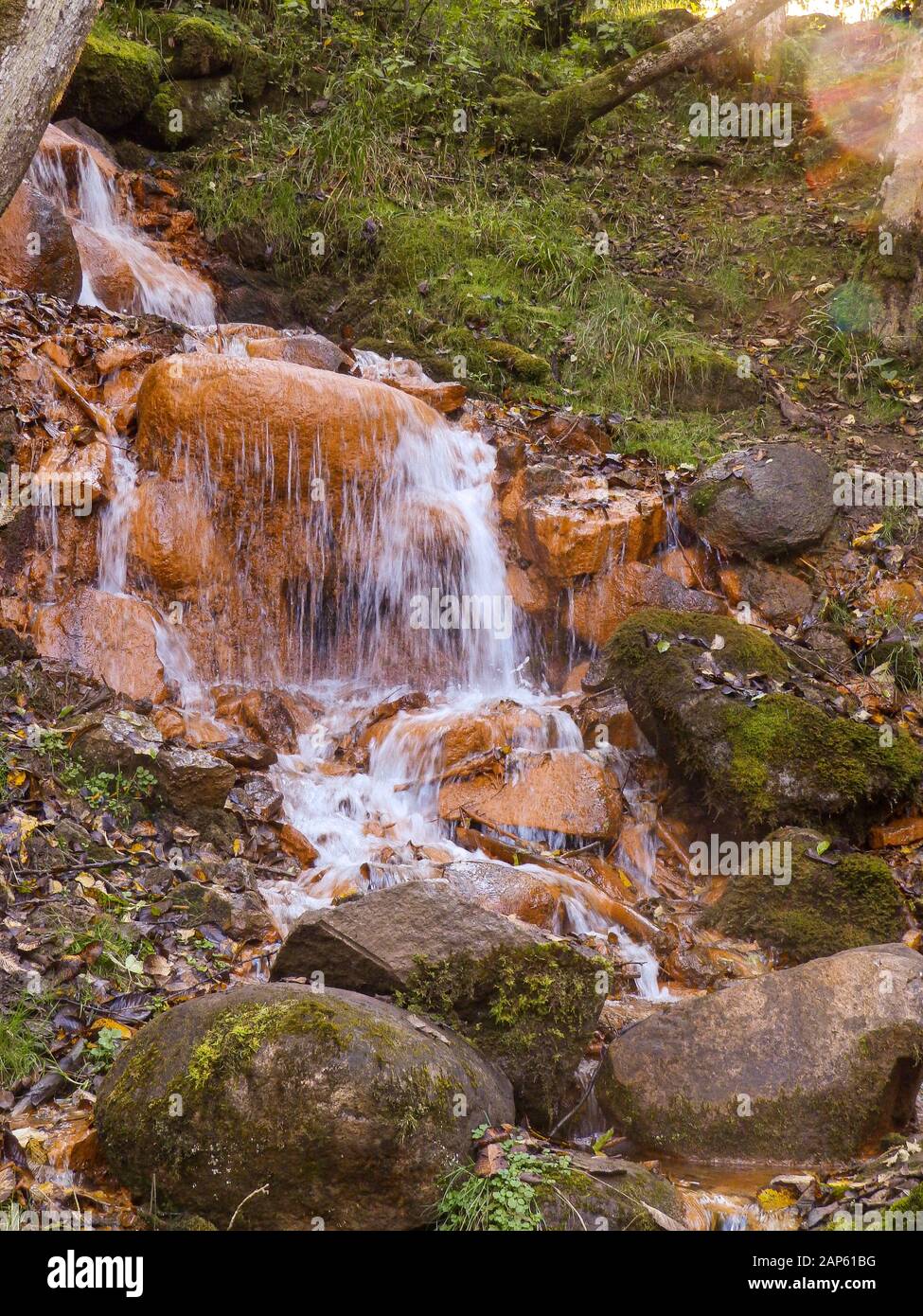 wild landscape with a small waterfall, running water in orange tones ...