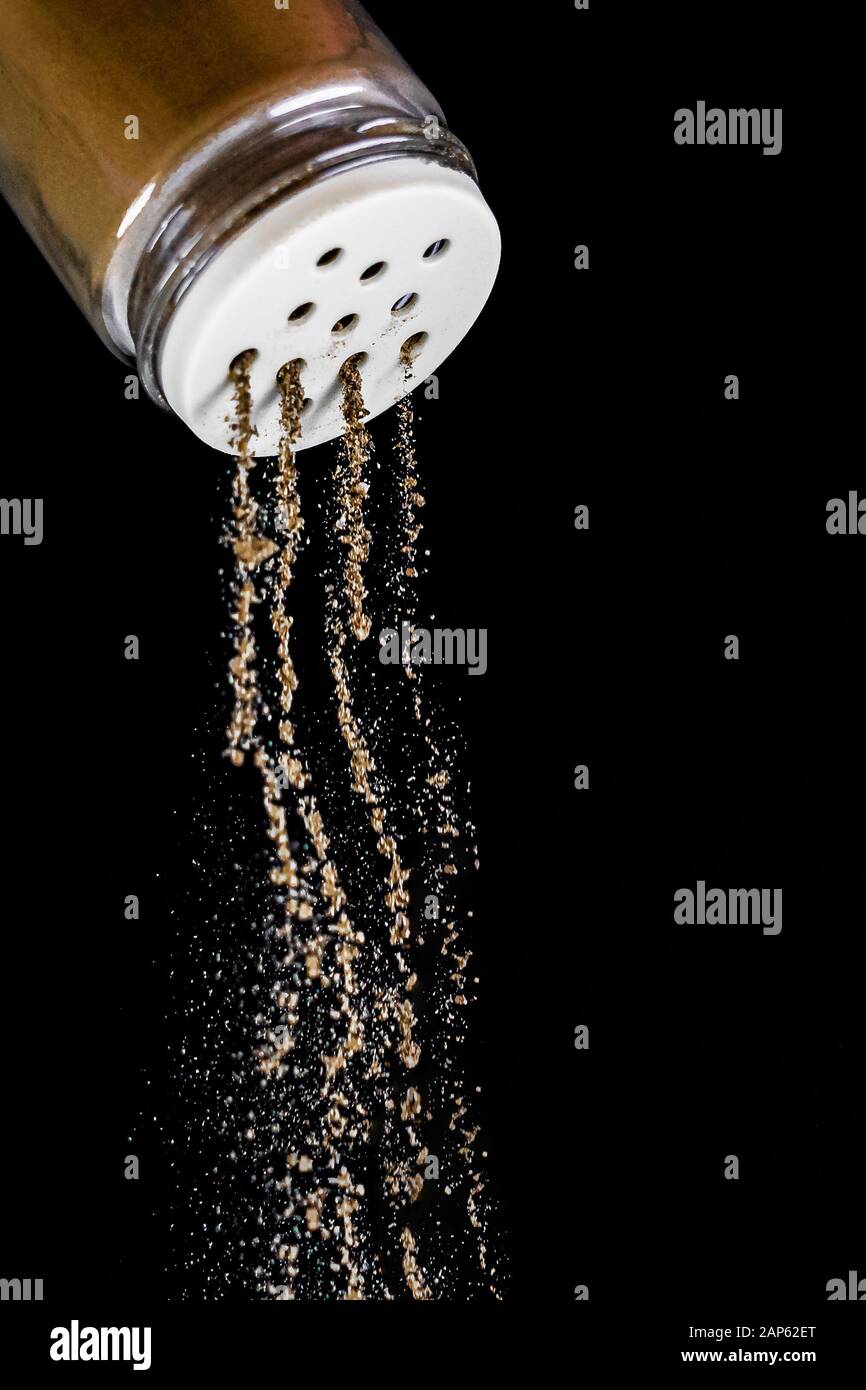 Black ground pepper falls out of the pepper shaker on a black isolated ...