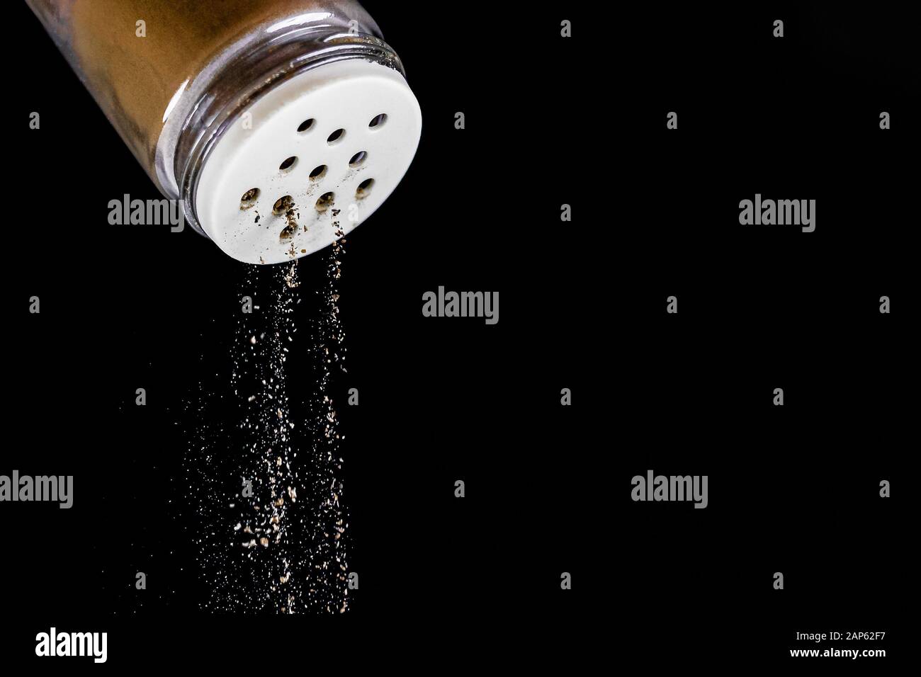 Black ground pepper falls out of the pepper shaker on a black isolated ...