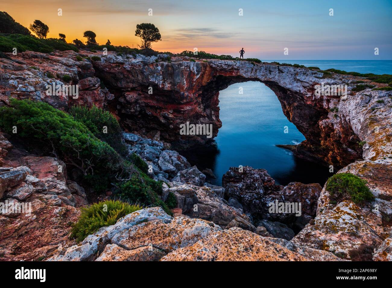 Silhouette of a man on Cala Varques, natural bridge above sea water ...