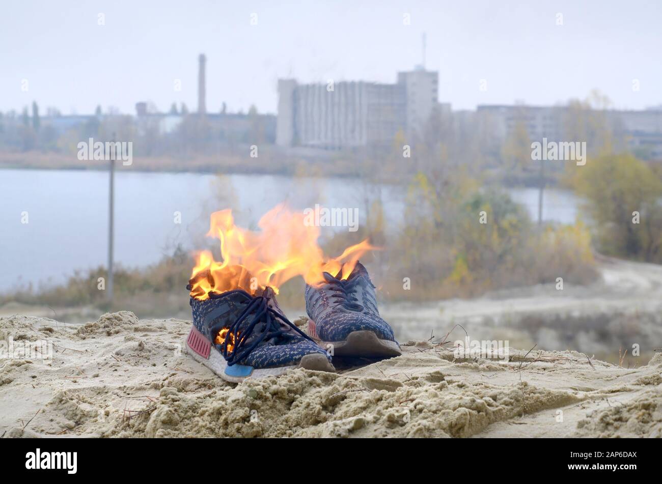 Burning sports sneakers or gym shoes on fire stand on sandy beach coast ...