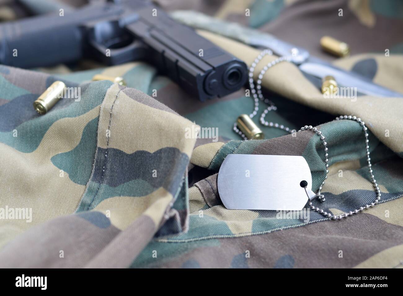 Army Dog tag token with 9mm bullets and pistol lie on folded camouflage ...
