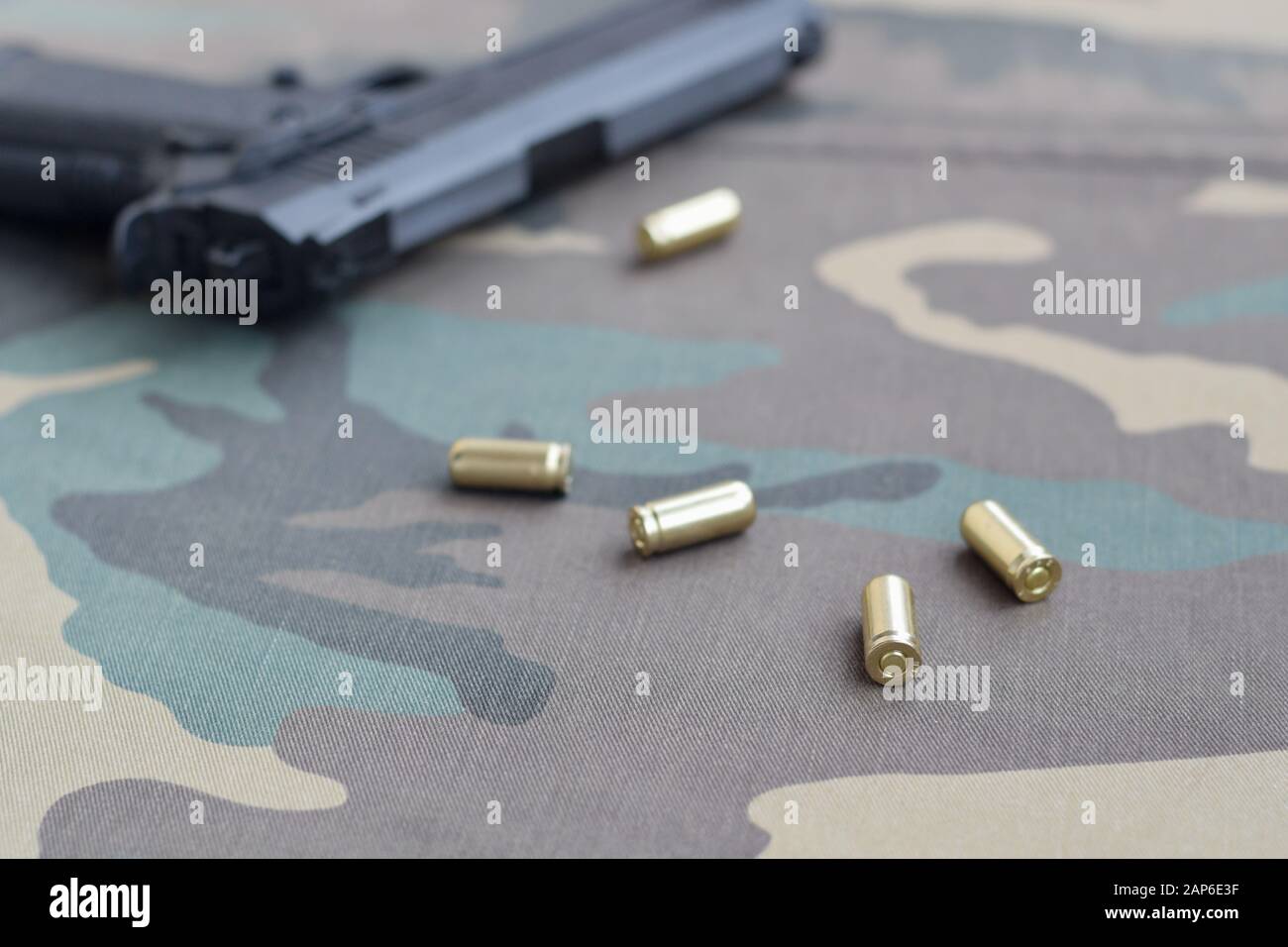 9mm bullets and pistol lie on camouflage green fabric. A set shooting ...
