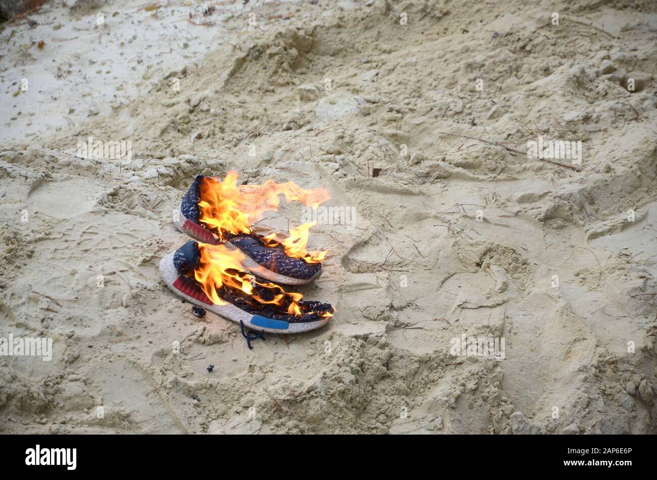 Burning sports sneakers or gym shoes on fire stand on sandy beach coast ...