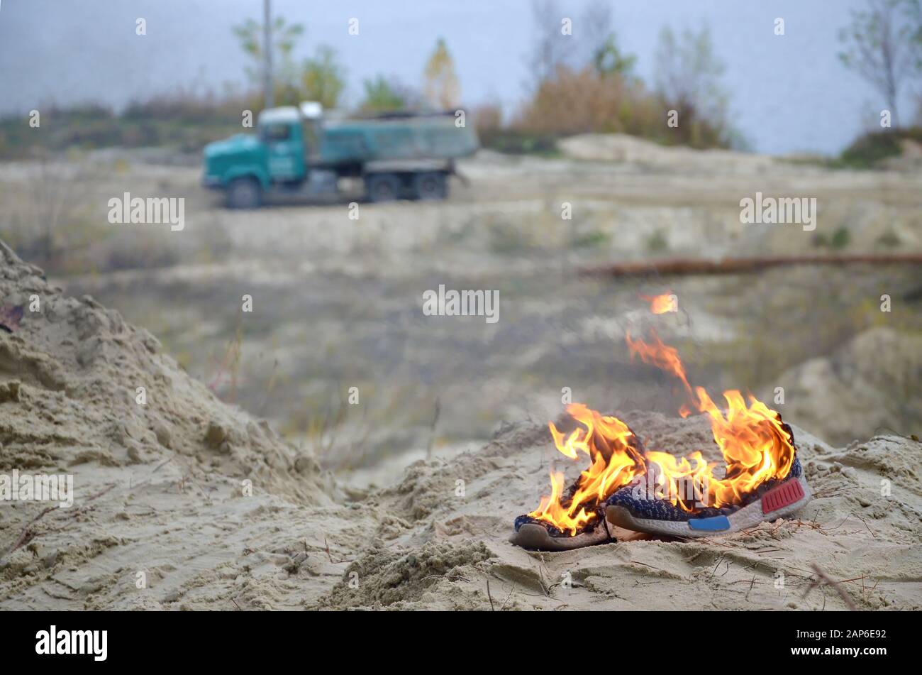 Burning sports sneakers or gym shoes on fire stand on sandy beach coast ...